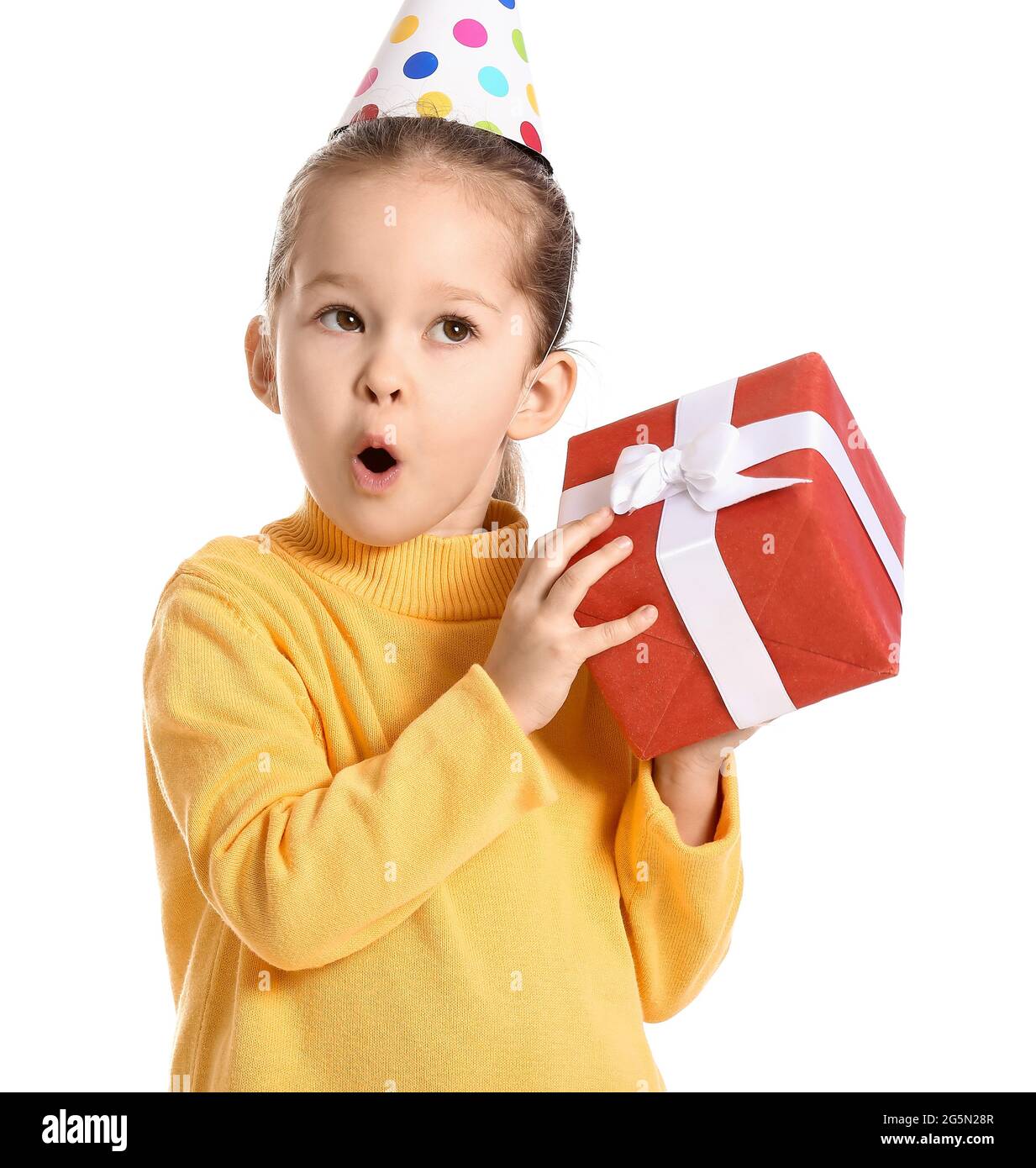 Surprised little girl in party hat with gift box on white background ...