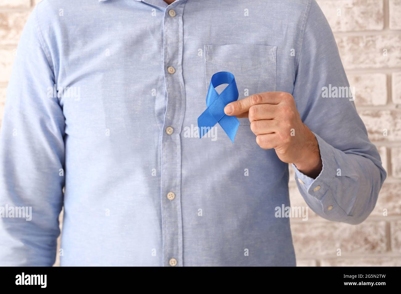 Man with blue ribbon near light brick wall, closeup. Colon cancer ...