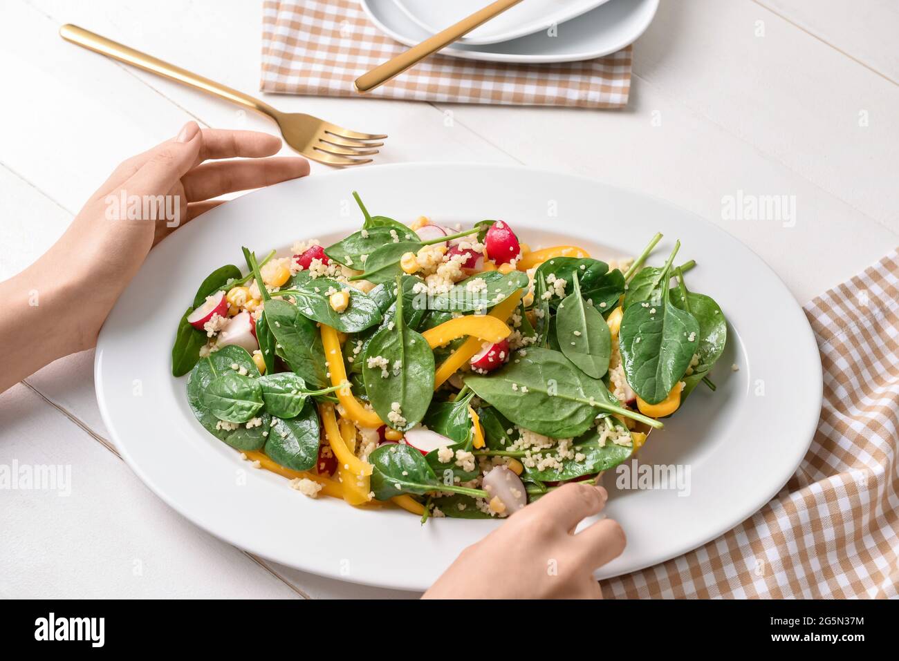 Woman eating tasty couscous with vegetables on light wooden background ...