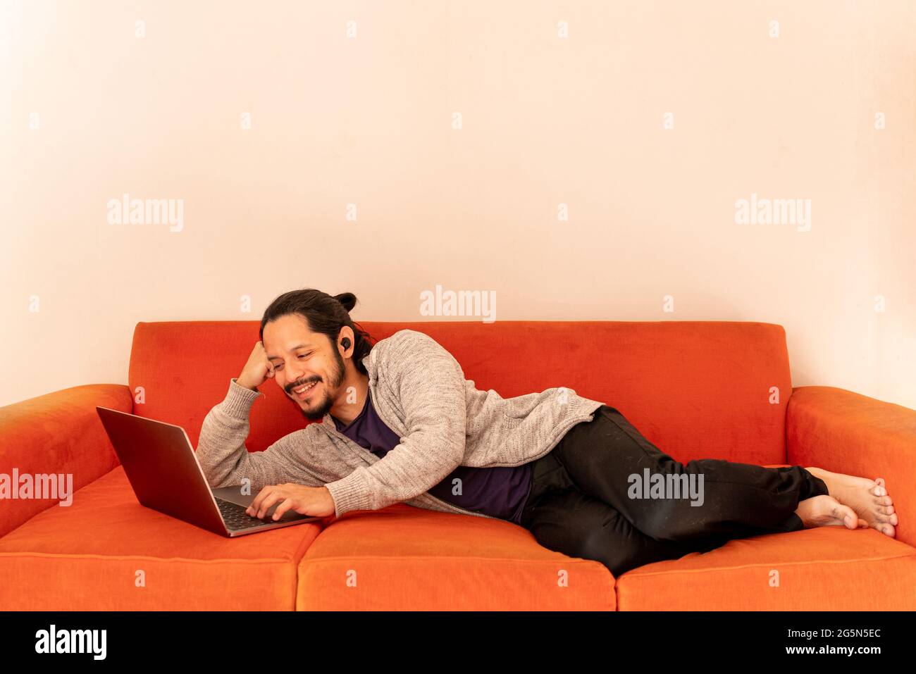 Young man dating online using the computer laptop laying on an orange ...