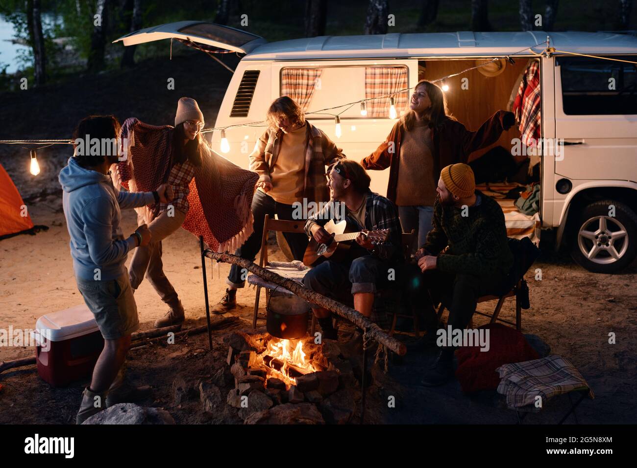Group of young people dancing together around the fire during camping ...