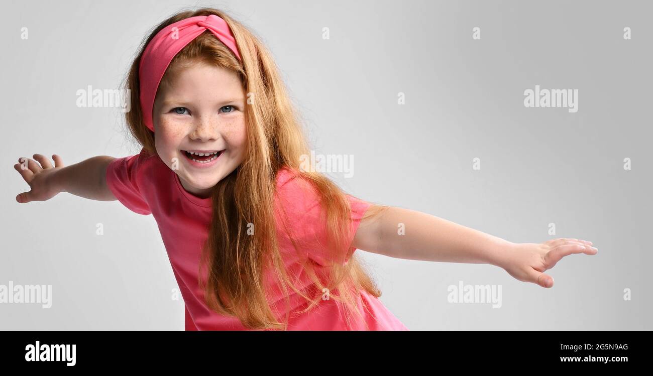 Laughing redhead kid girl in pink t-shirt stands holding hands spread ...