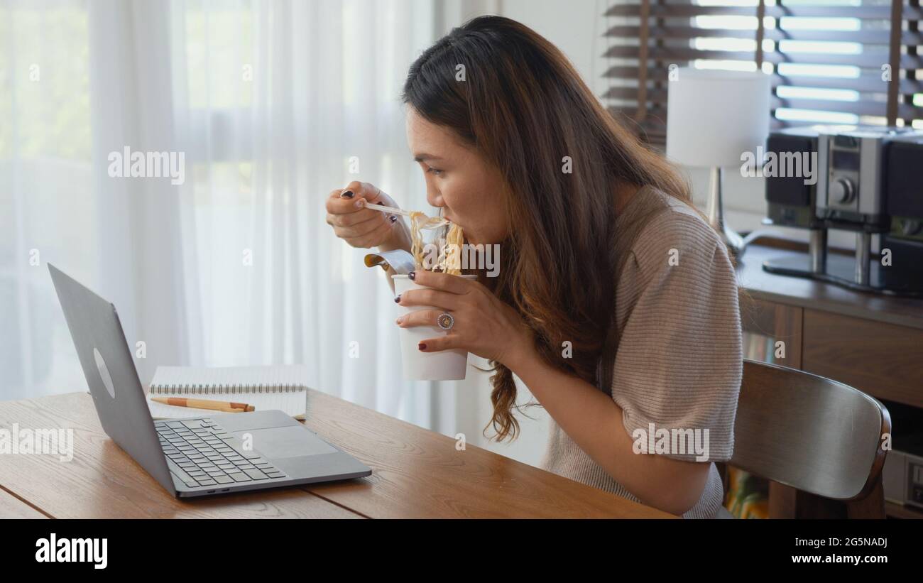 Asian business woman eating instant noodles while working on laptop ...