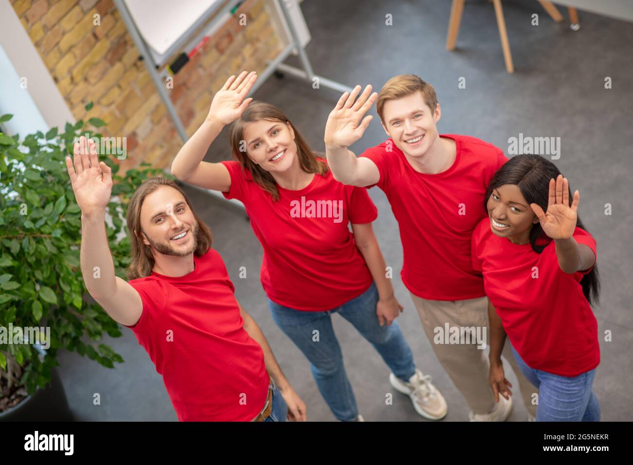 Team of young volunteers waving hand while standing indoors Stock Photo ...