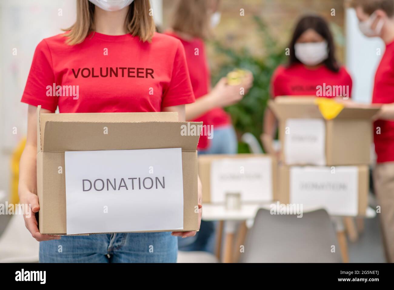 Volunteer girl holding donation box and friends behind Stock Photo - Alamy
