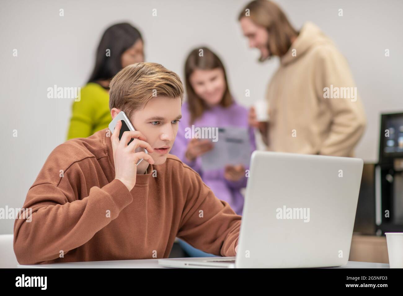 Guy talking on smartphone at laptop and colleagues Stock Photo - Alamy