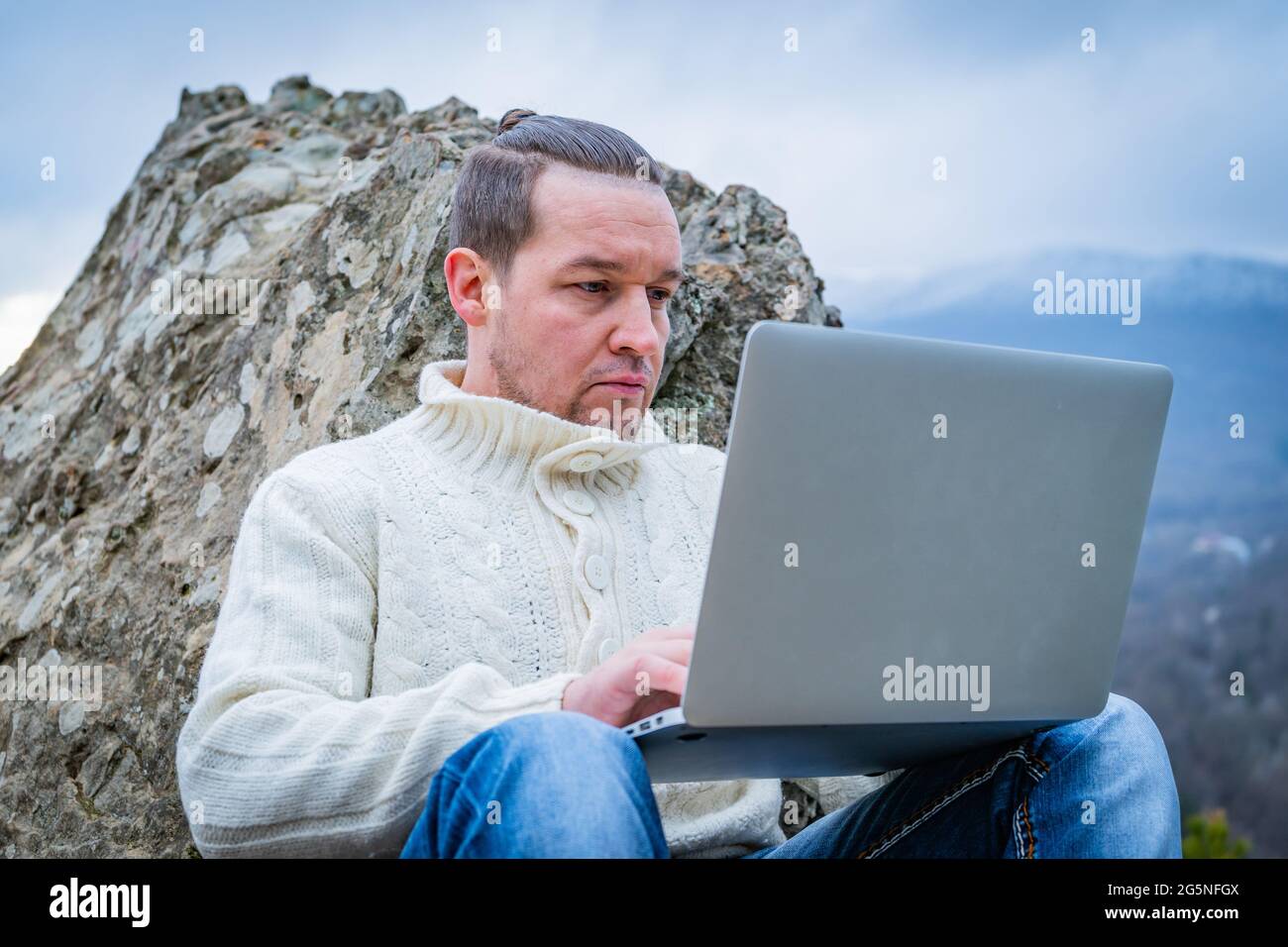 Blogger man sitting on a rock ad using a laptop Stock Photo - Alamy