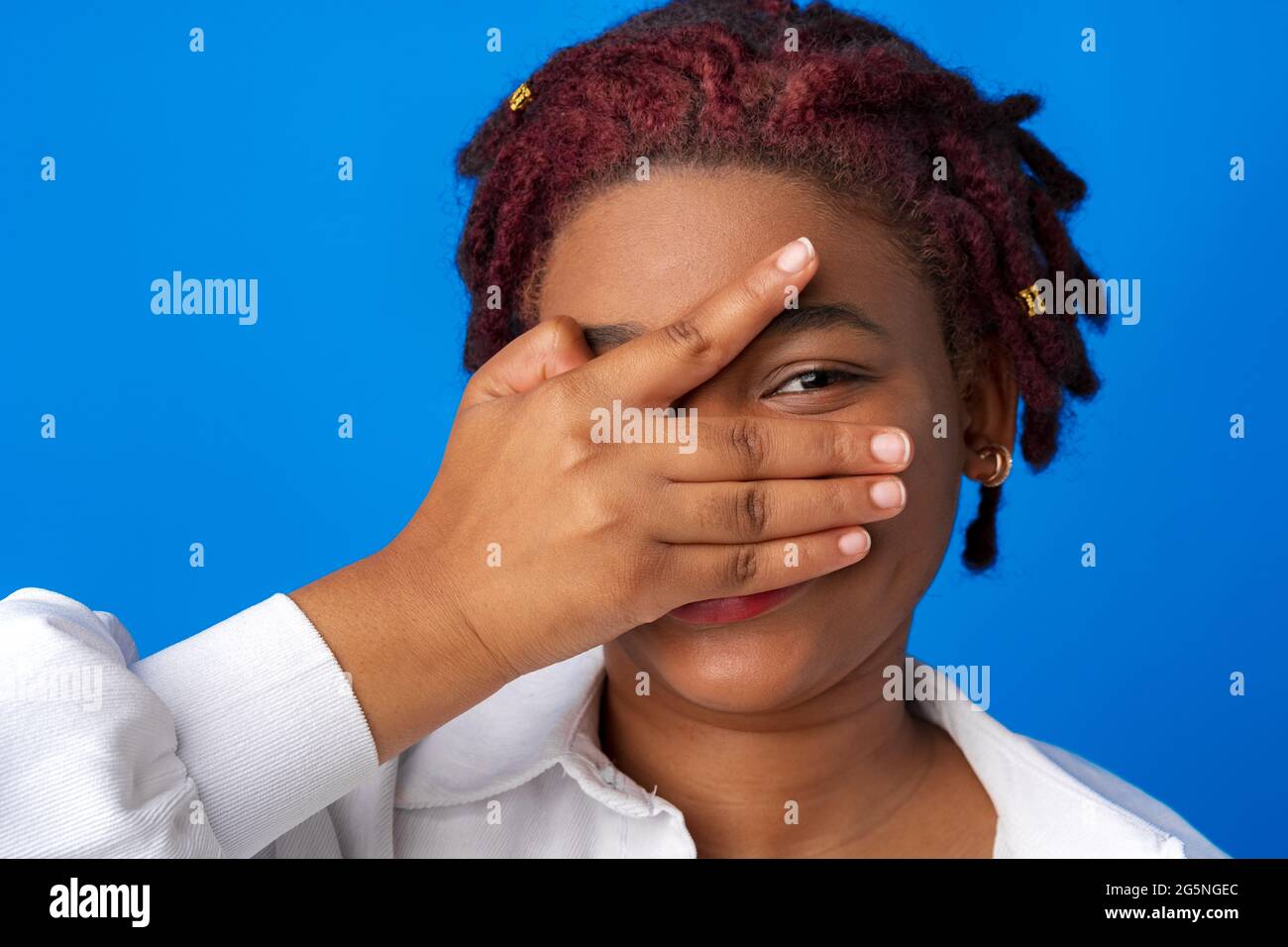 Funny afro woman peeping through the palm of her hand against blue ...