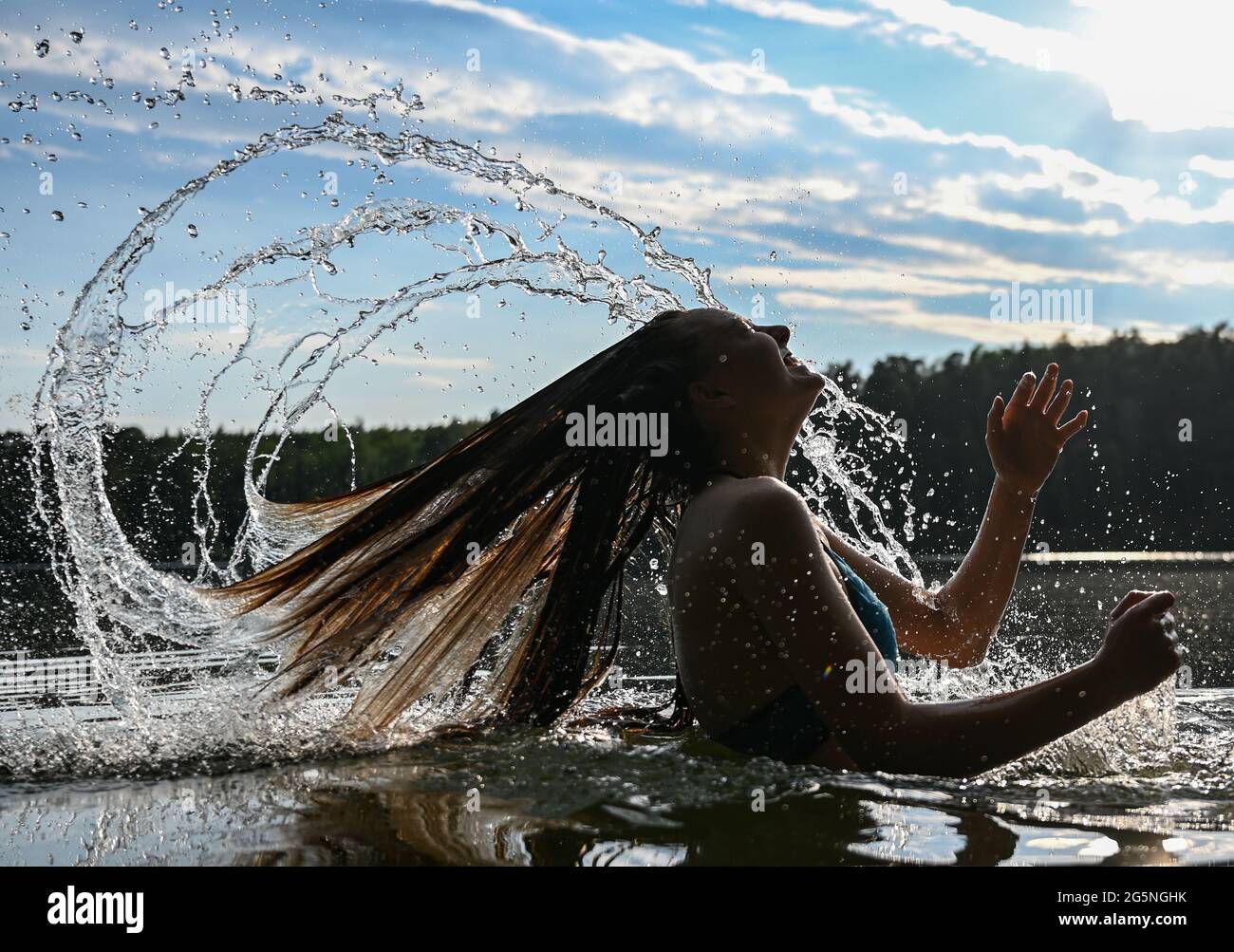 Treplin, Germany. 28th June, 2021. A girl stands in a lake and shakes ...