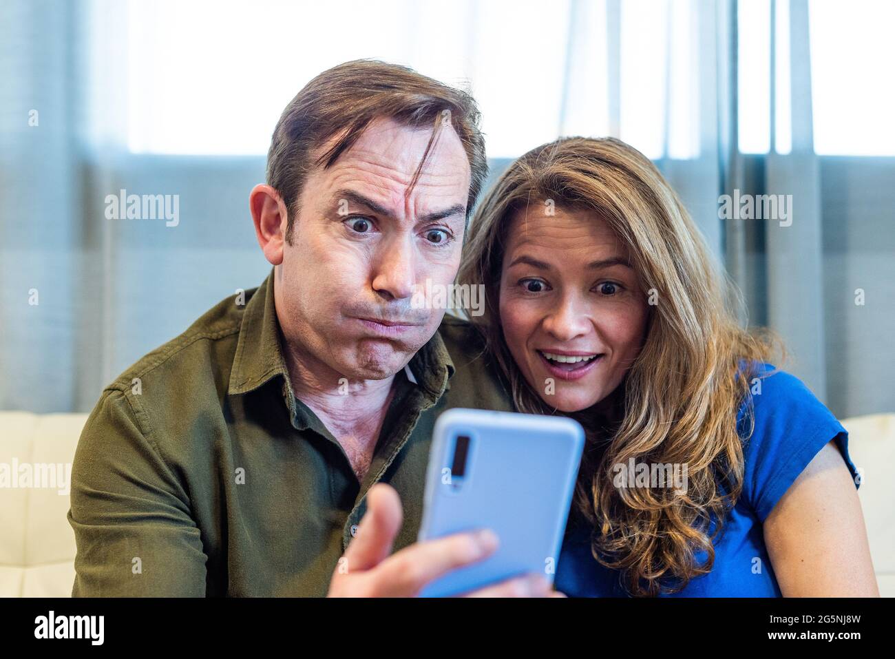 Mature couple at home watching something surprising on mobile Stock ...