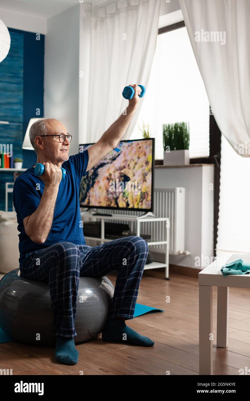 Retirement senior man sitting on aerobics swiss ball raising hand ...