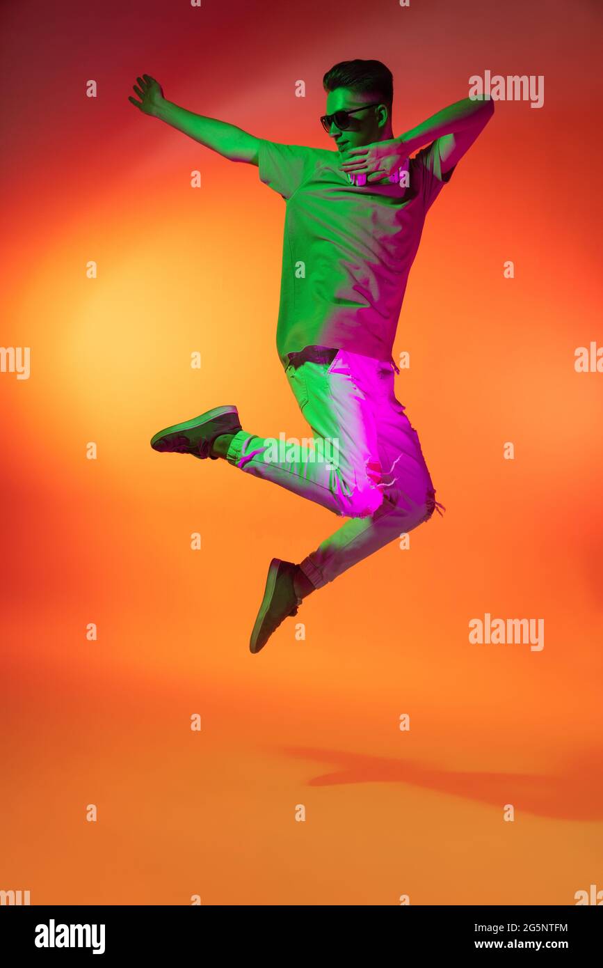 Portrait of Caucasian young man jumping, dancing isolated on orange ...