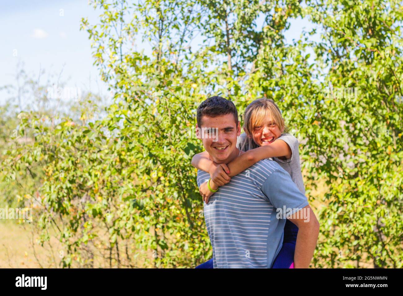 Defocused brother giving sister ride on back. Portrait of happy girl on ...
