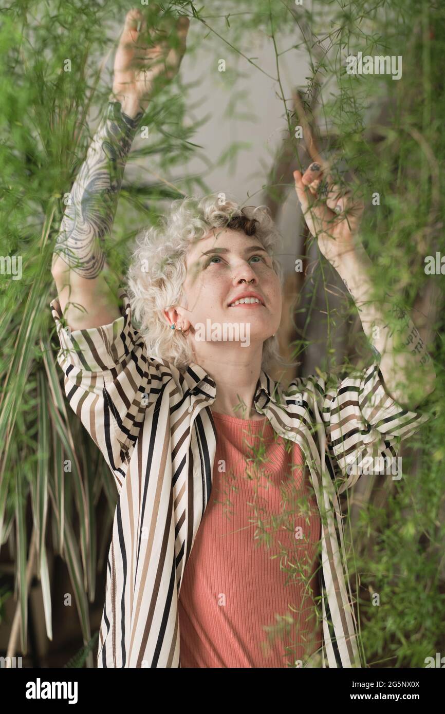 Young florist raising her hands and caring about green plants in flower ...