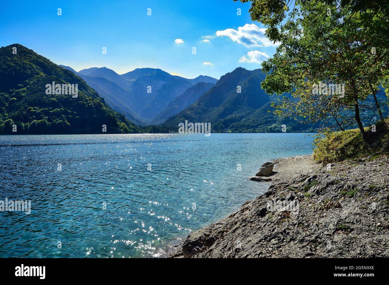 crystal blue water of lake Ledro, stone beach, rocks, mountains, branch ...