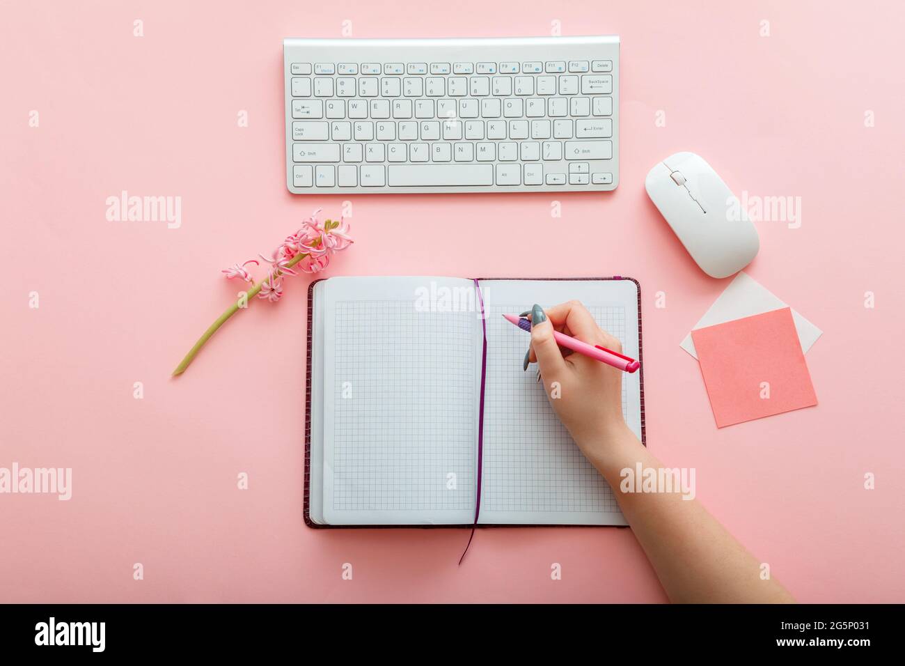 Pink work desk with female hand writes notes in notebook at workplace ...