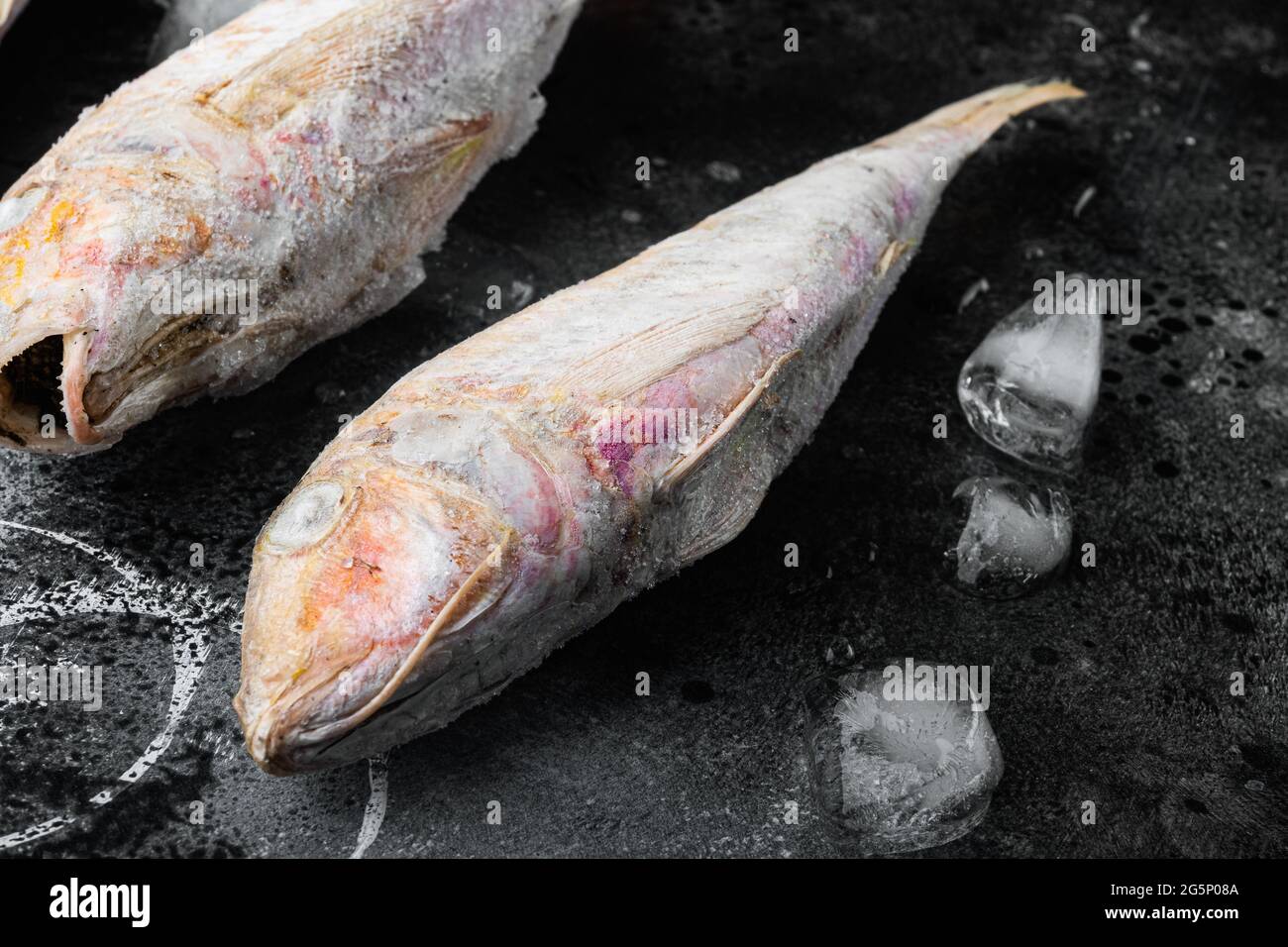 Frozen red mullet or barabulka raw fish set, on black dark stone table ...