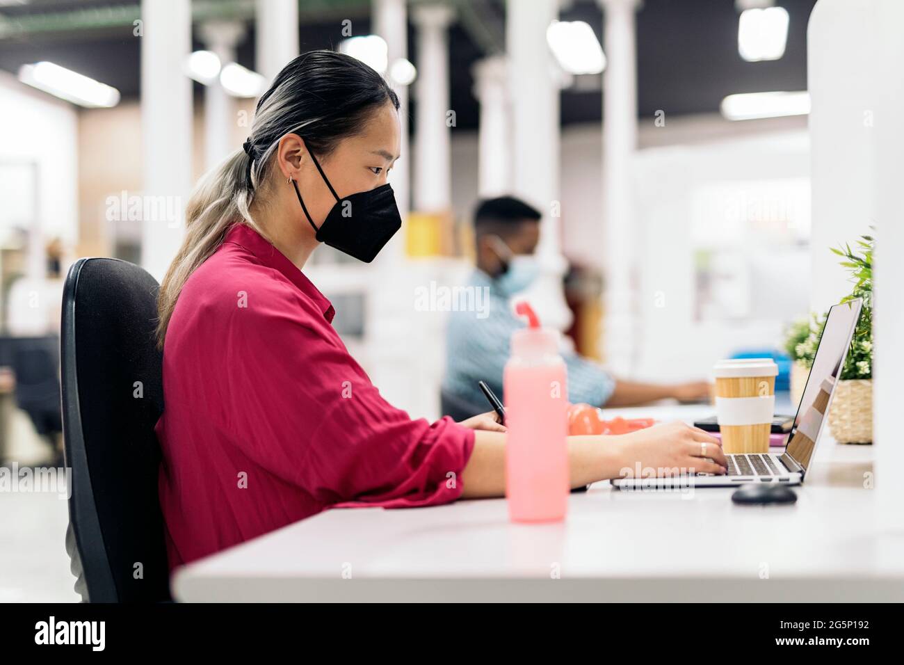 Concentrated asian office worker with face mask sitting in her desk and ...