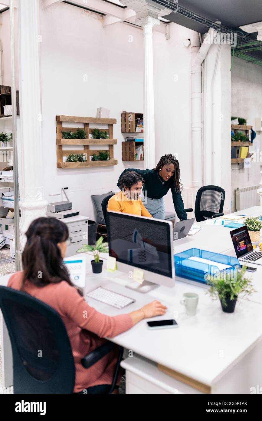 Diverse office workers sitting in a big desk and working with laptops ...