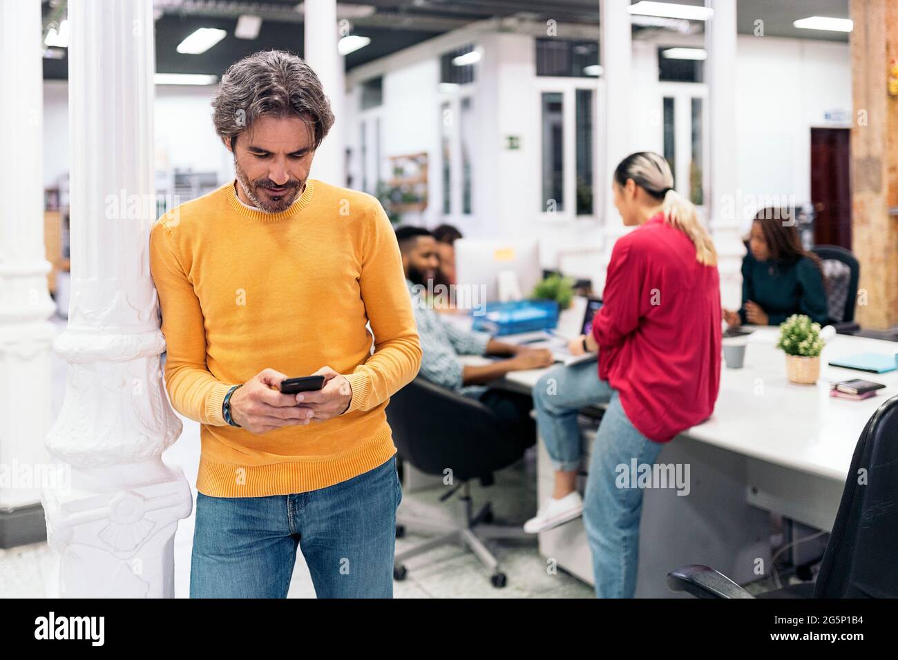 Smiley male office worker using his mobile phone and standing in the ...