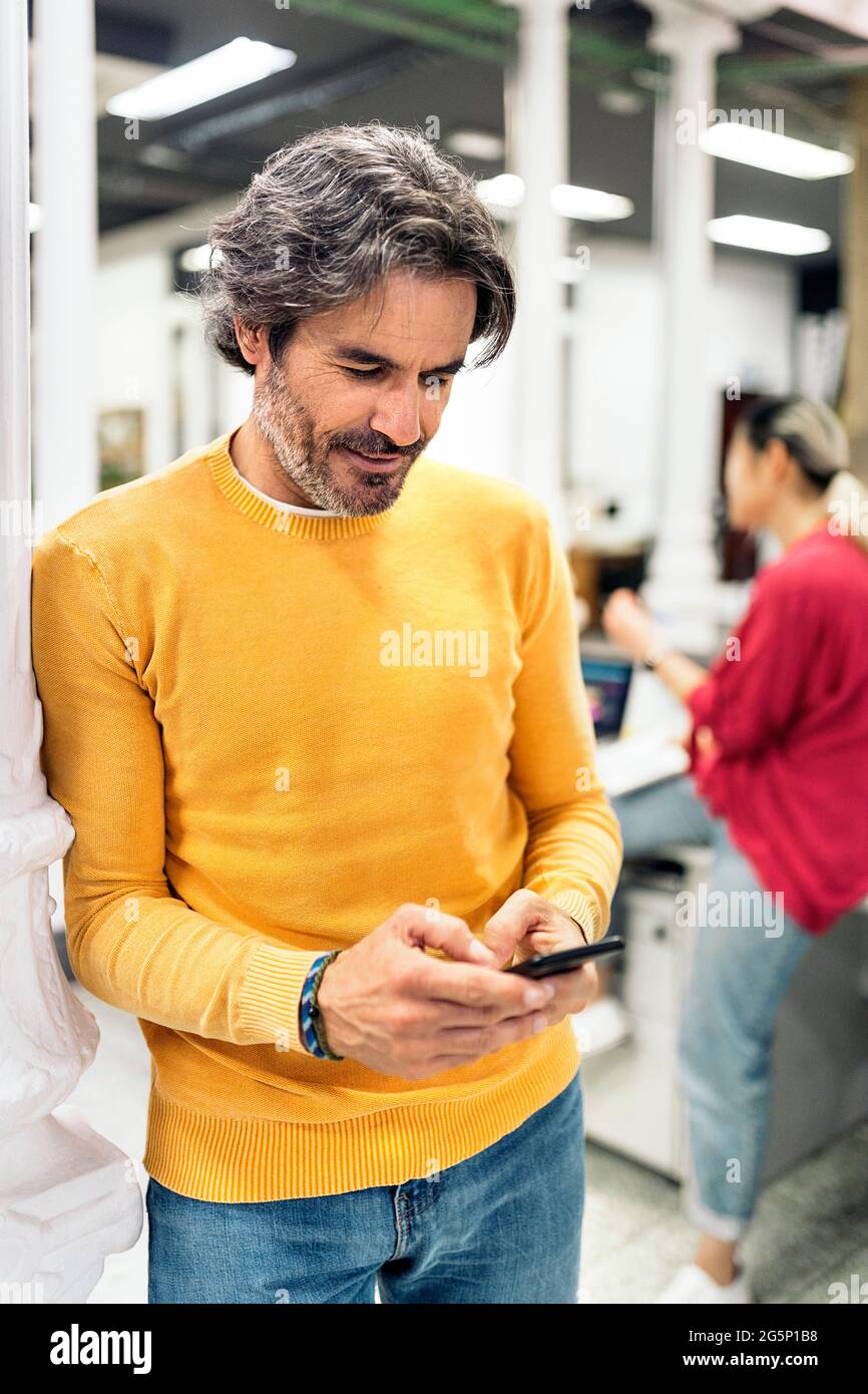 Smiley male office worker using his mobile phone and standing in the ...