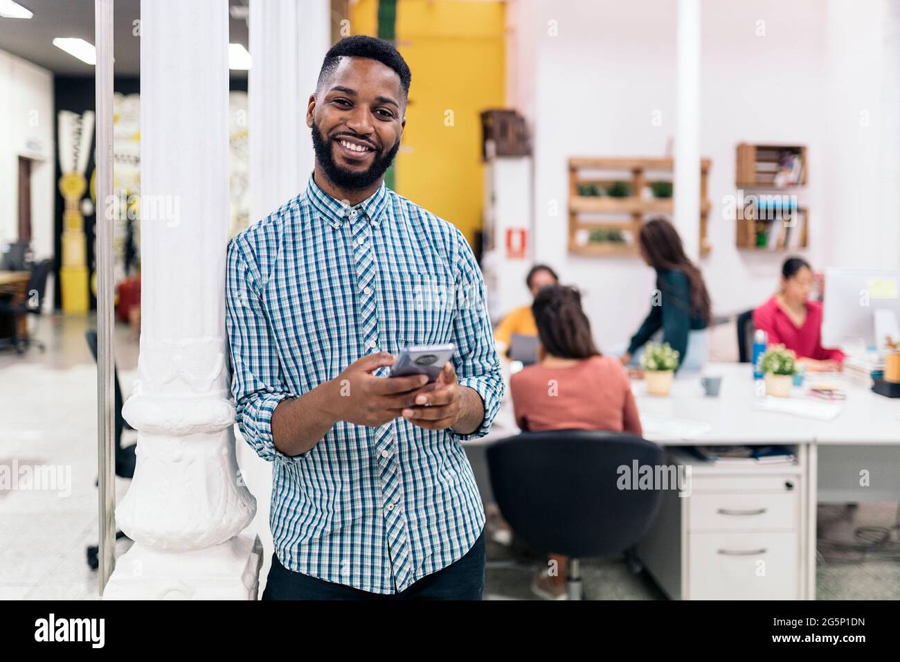 Smiley african office worker holding his mobile phone and looking at ...