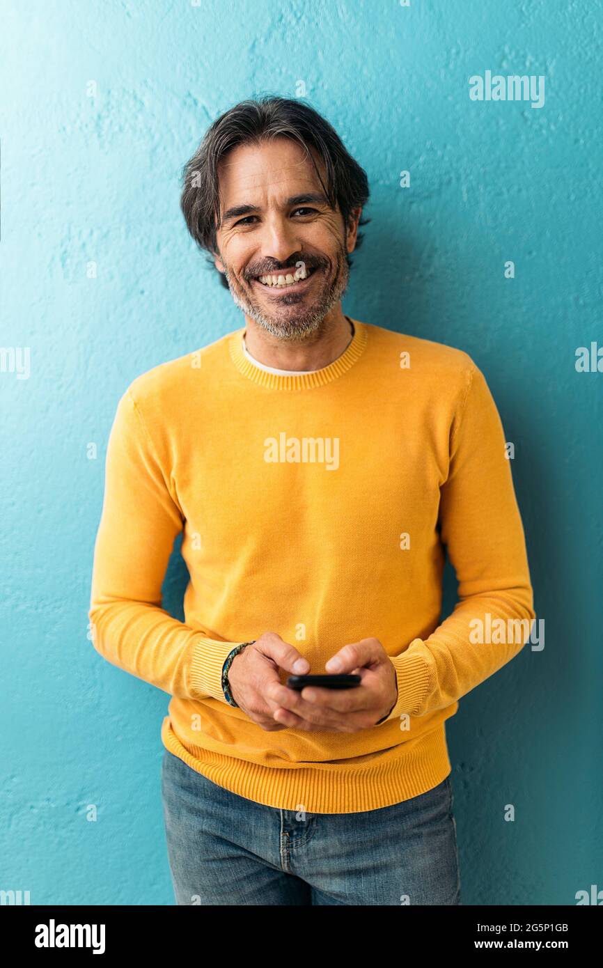 Smiley male office worker holding his mobile phone and looking at ...