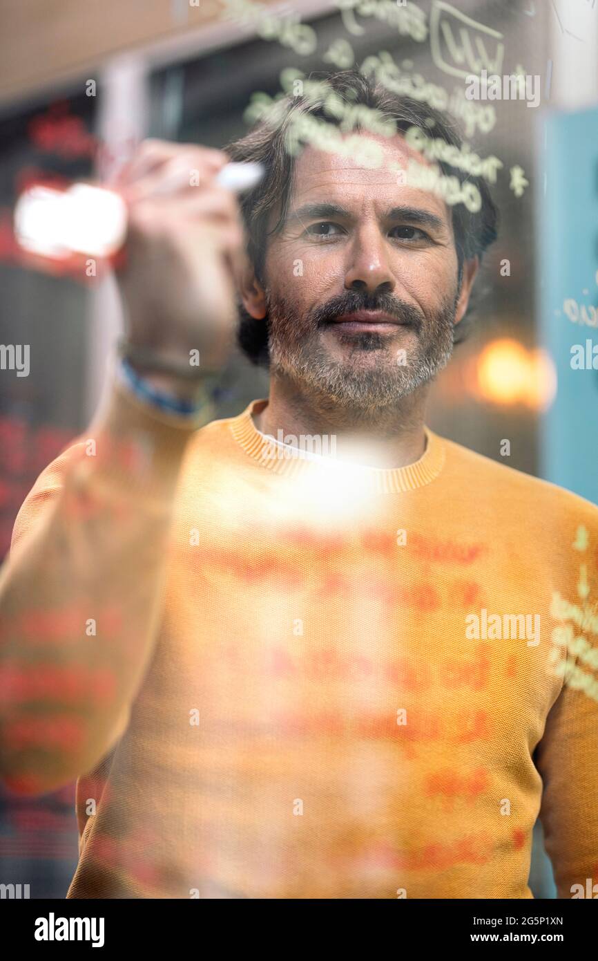 Bearded male office worker writing in white board and smiling. Co ...