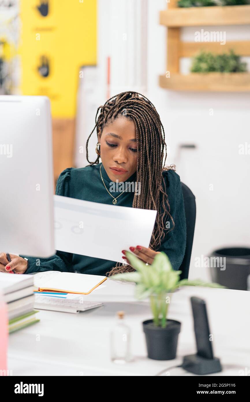 Focused black woman sitting in her desk and doing paper work. Office ...