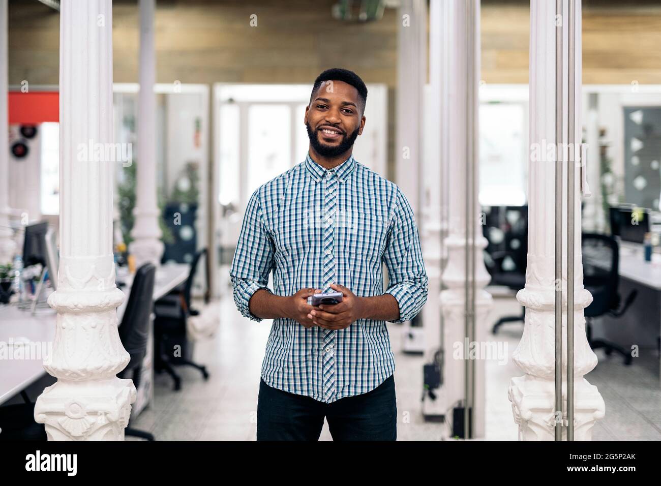 Smiley african office worker holding his mobile phone and looking at ...