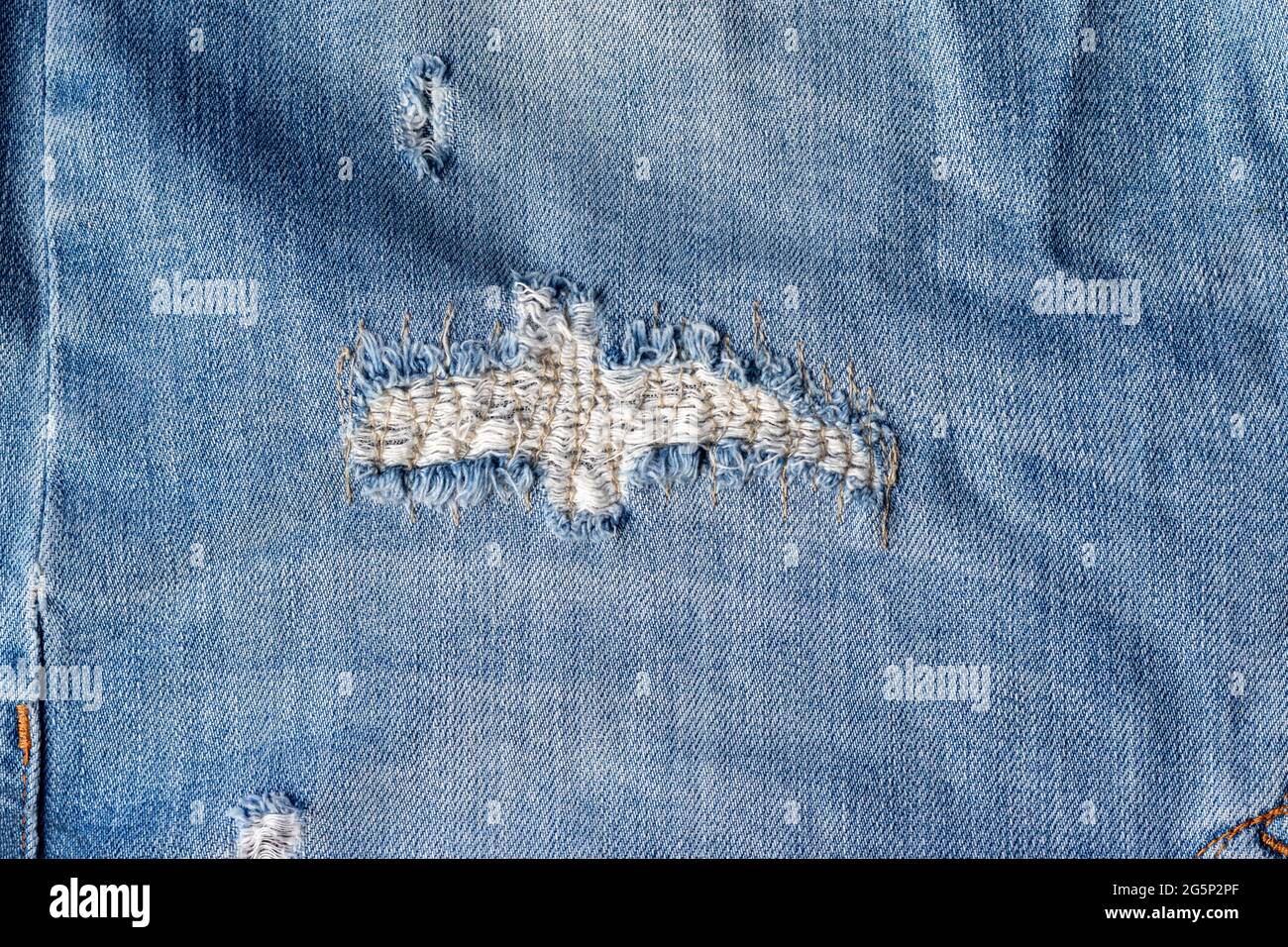 Blue torn jeans fabric texture. Distressed denim with sewn-up hole and ...