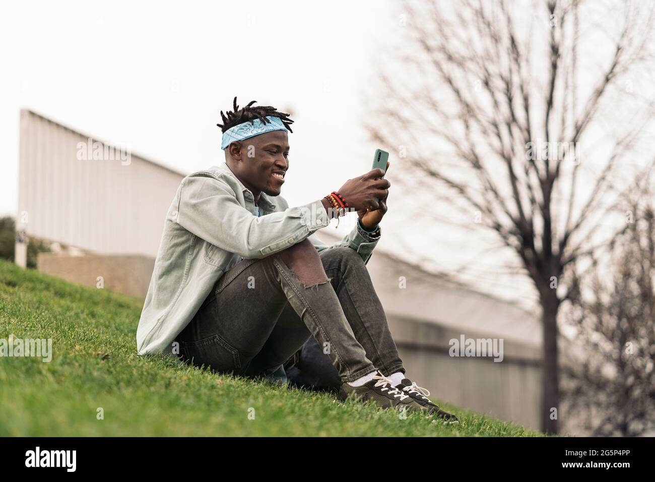 Handsome and cool african man sitting in the grass and using his ...