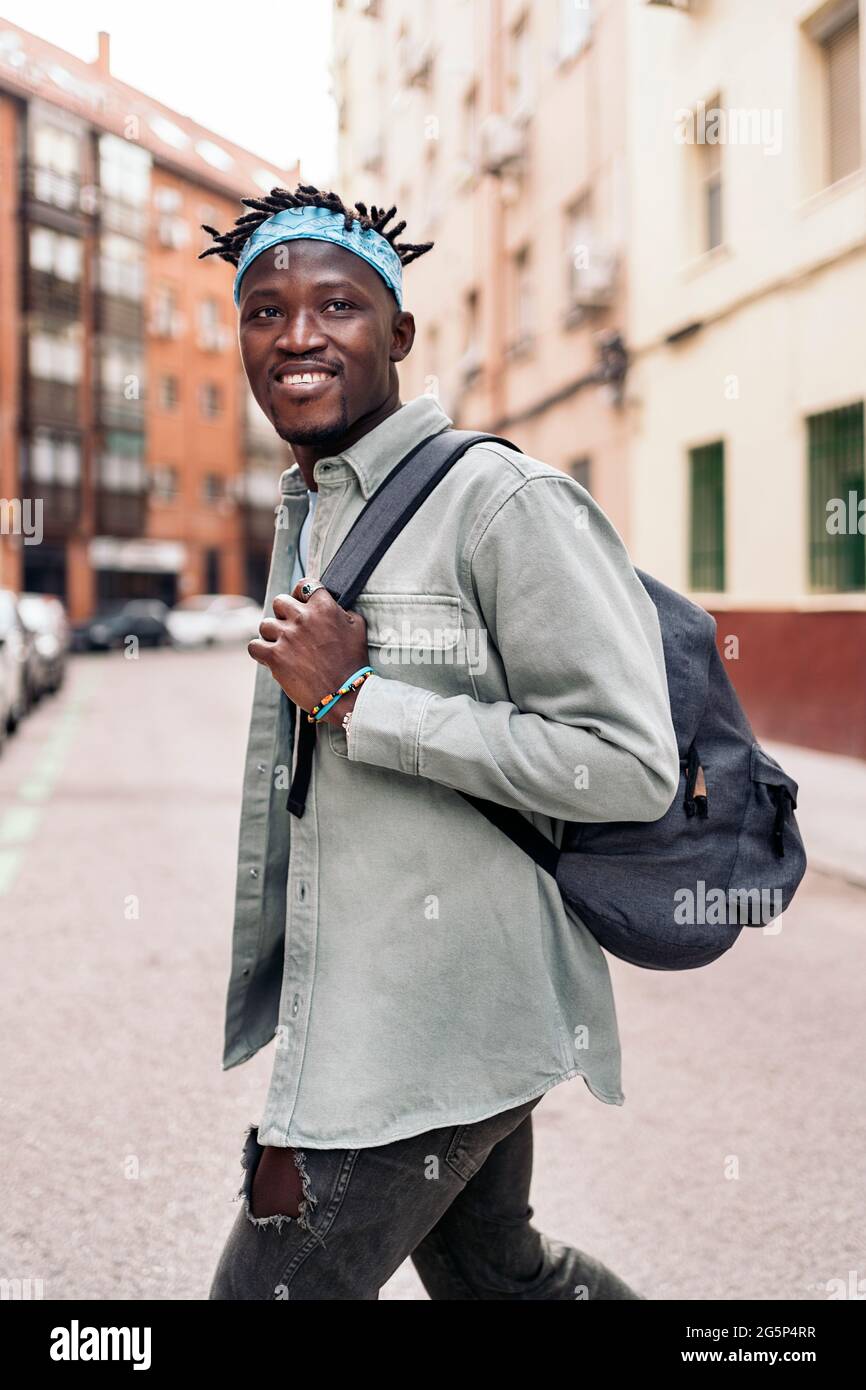 Attractive african boy with dreadlocks and wearing backpack walking in ...