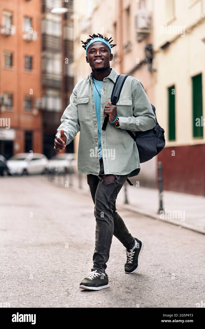 Attractive african boy with dreadlocks and wearing backpack walking in ...