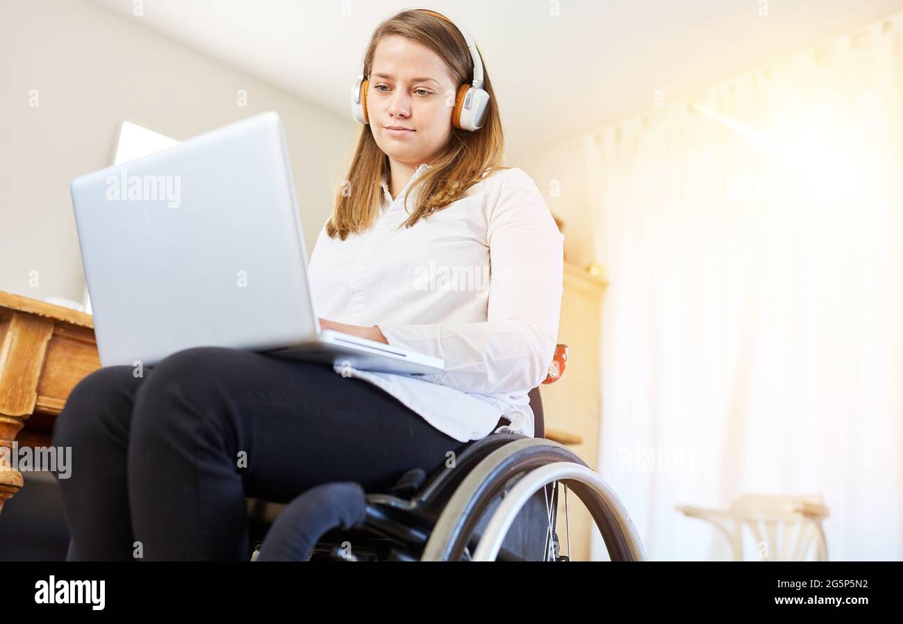 Disabled woman in wheelchair working on laptop computer in home office ...