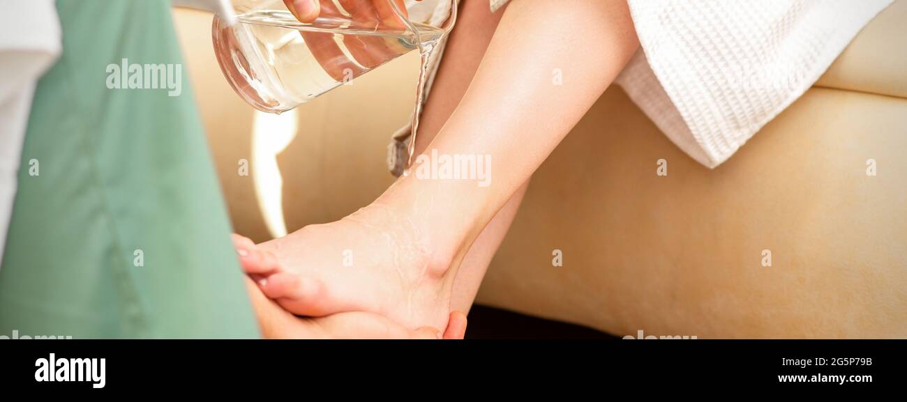 Close up of hands of male therapist washing legs of a young woman in ...