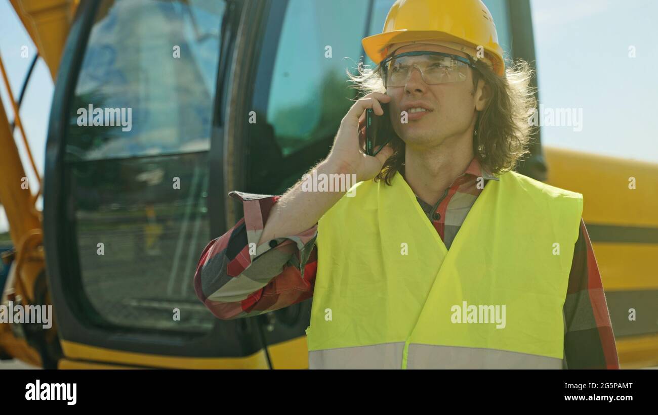 Excavator operator in hard hat talking by smartphone Stock Photo - Alamy