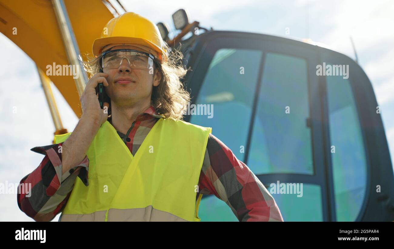 Excavator operator in hard hat talking by smartphone Stock Photo - Alamy