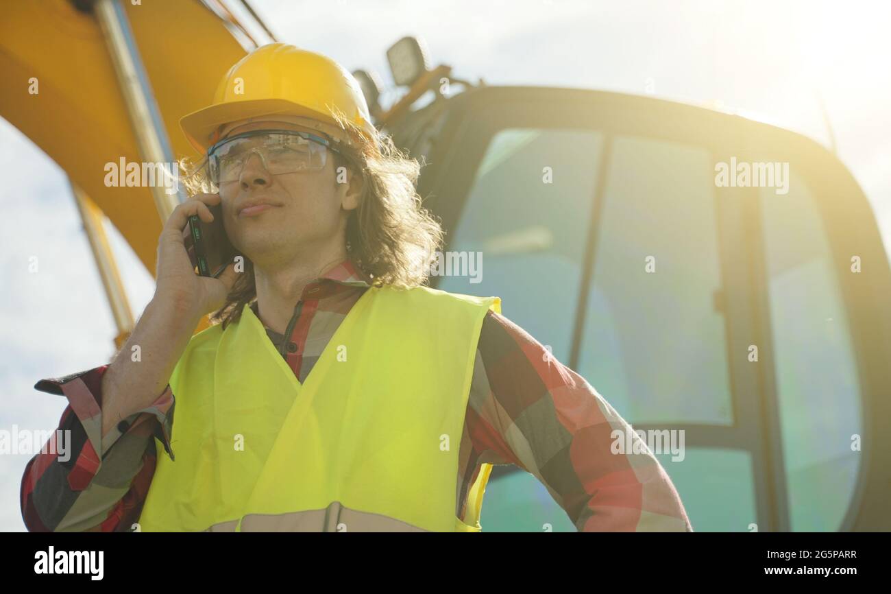 Excavator operator in hard hat talking by smartphone Stock Photo - Alamy