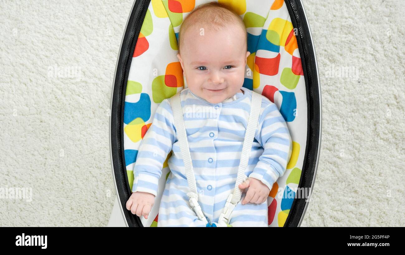 Cute smiling baby boy sitting in rocking chair and looking in camera ...