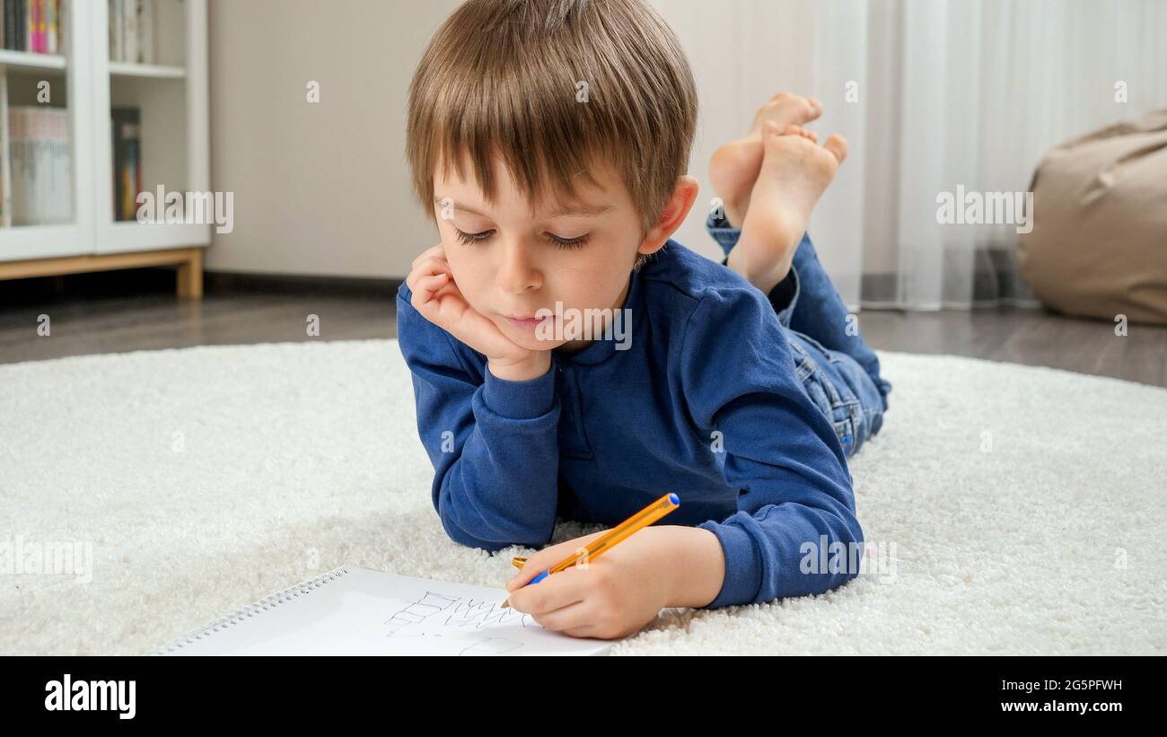 Little boy doing homework and writing in copybook on floor at home ...
