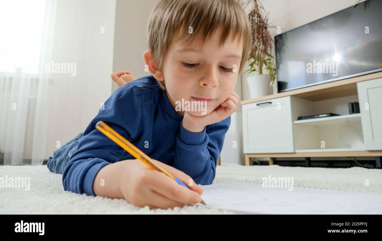 Little boy doing homework in copybook while lying on carpet in living ...