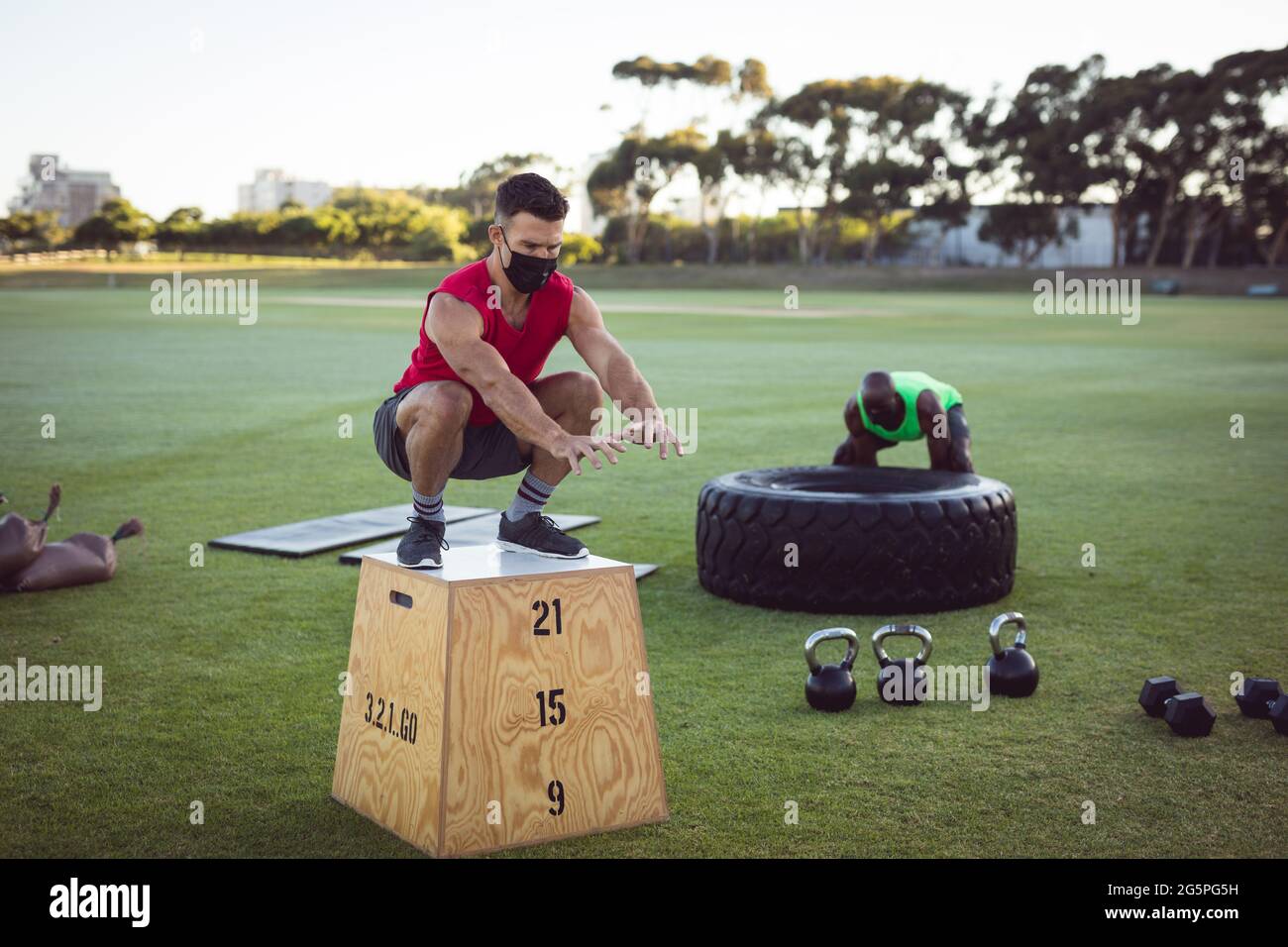 Fit caucasian man wearing face mask exercising outdoors, jumping onto ...
