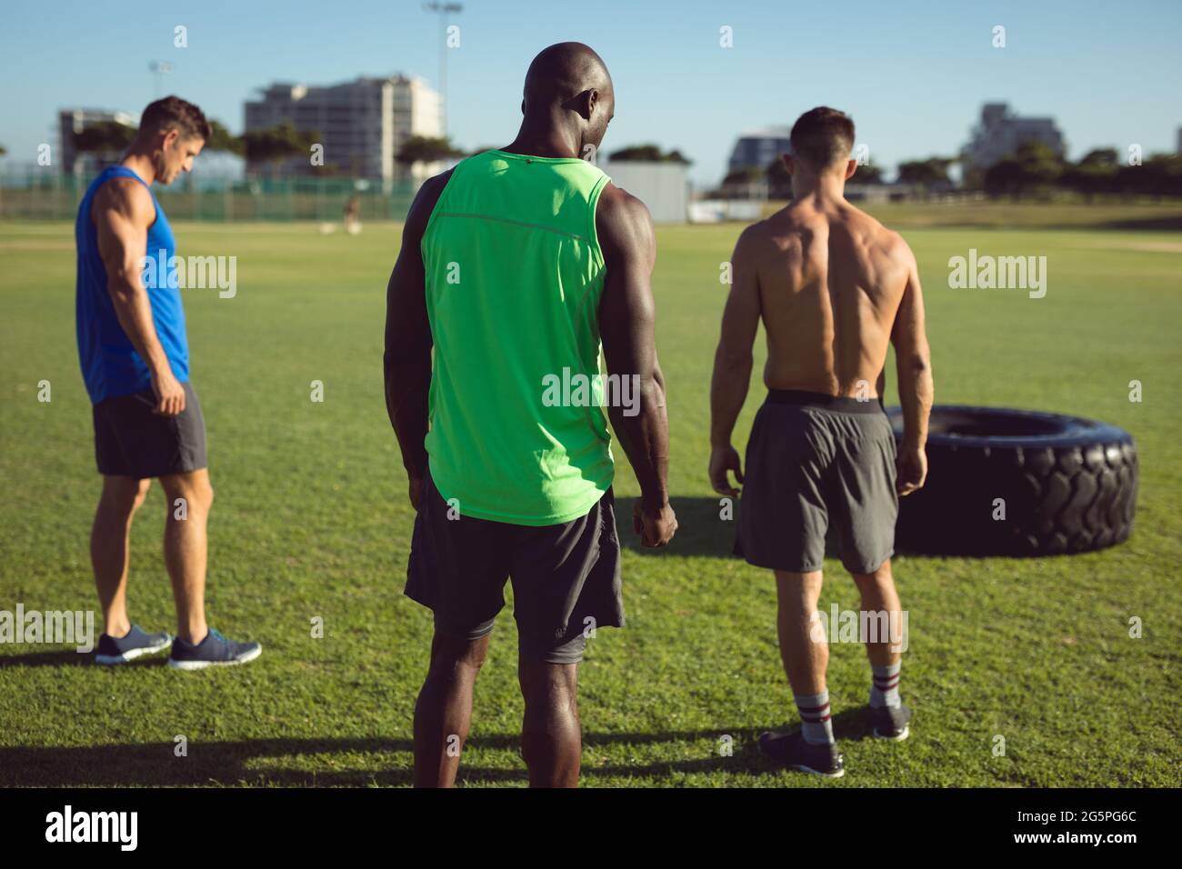 Three fit diverse men exercising outdoors, taking a break and catching ...