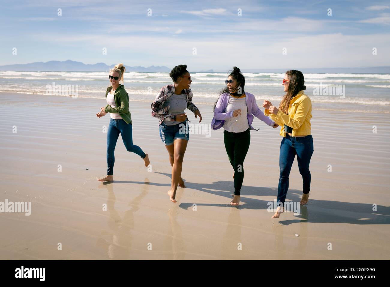 Happy group of diverse female friends having fun, walking along beach and laughing Stock Photo ...