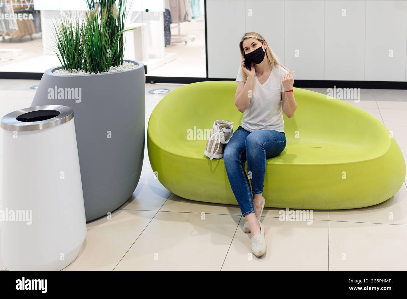 Beautiful blonde is talking on phone sitting in designer chair in mall ...