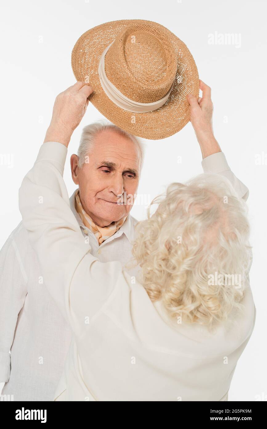 elderly woman putting hat on head of smiling husband isolated on white ...
