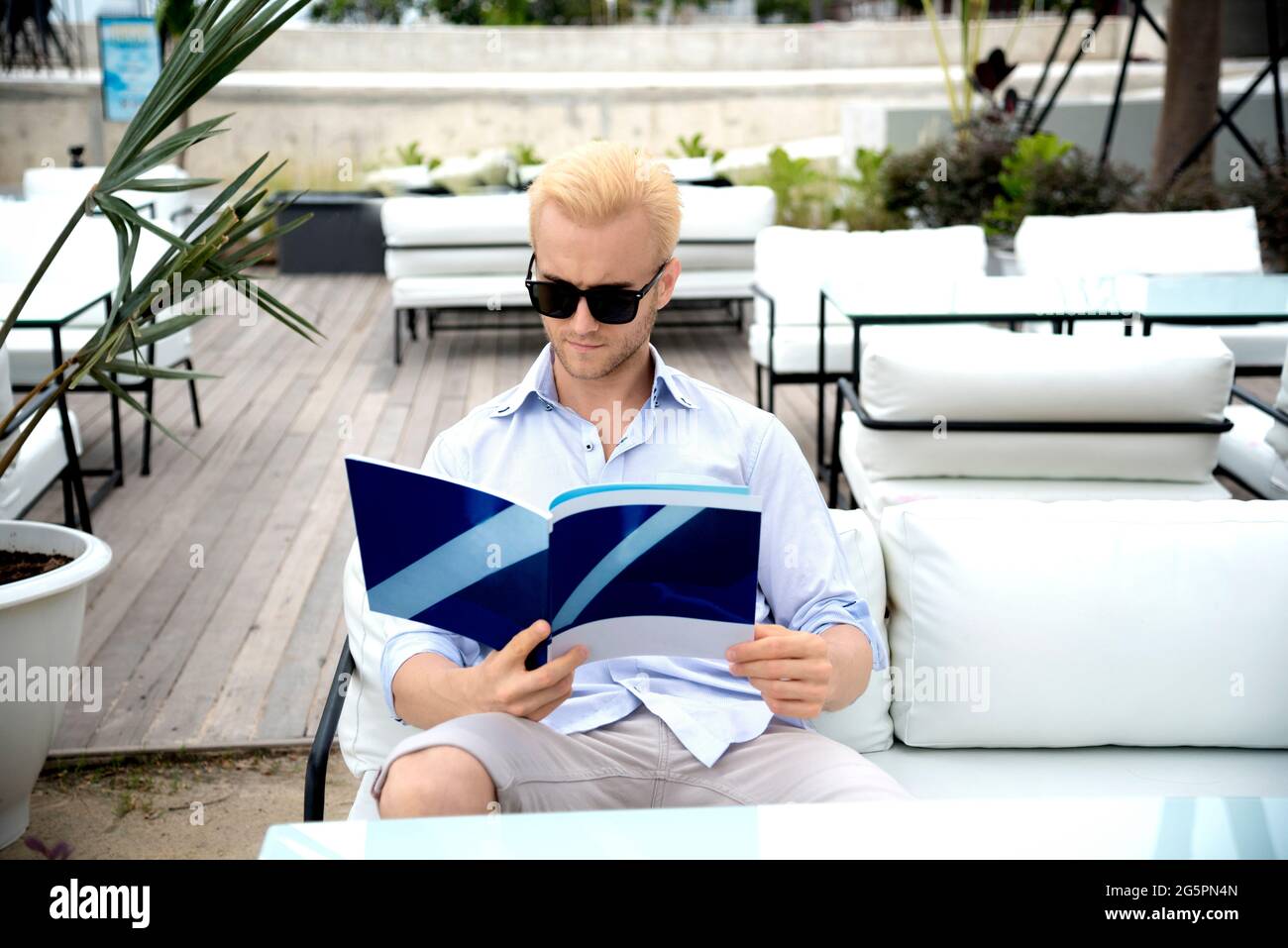 Caucasian young man reading magazine book on sofa reader holding a book ...
