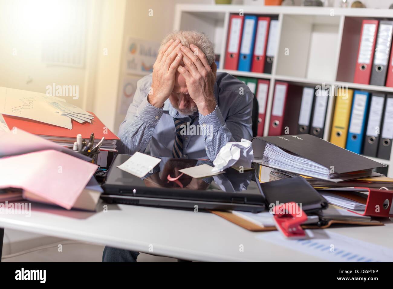 Overworked businessman sitting at a messy desk in office, light effect ...