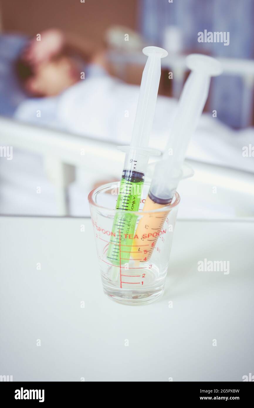 Syringes in a glass measuring cup with blurred illness boy lying on ...